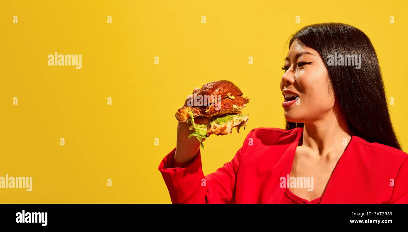 Side view of stylish young woman in red jacket preparing to bite giant ...