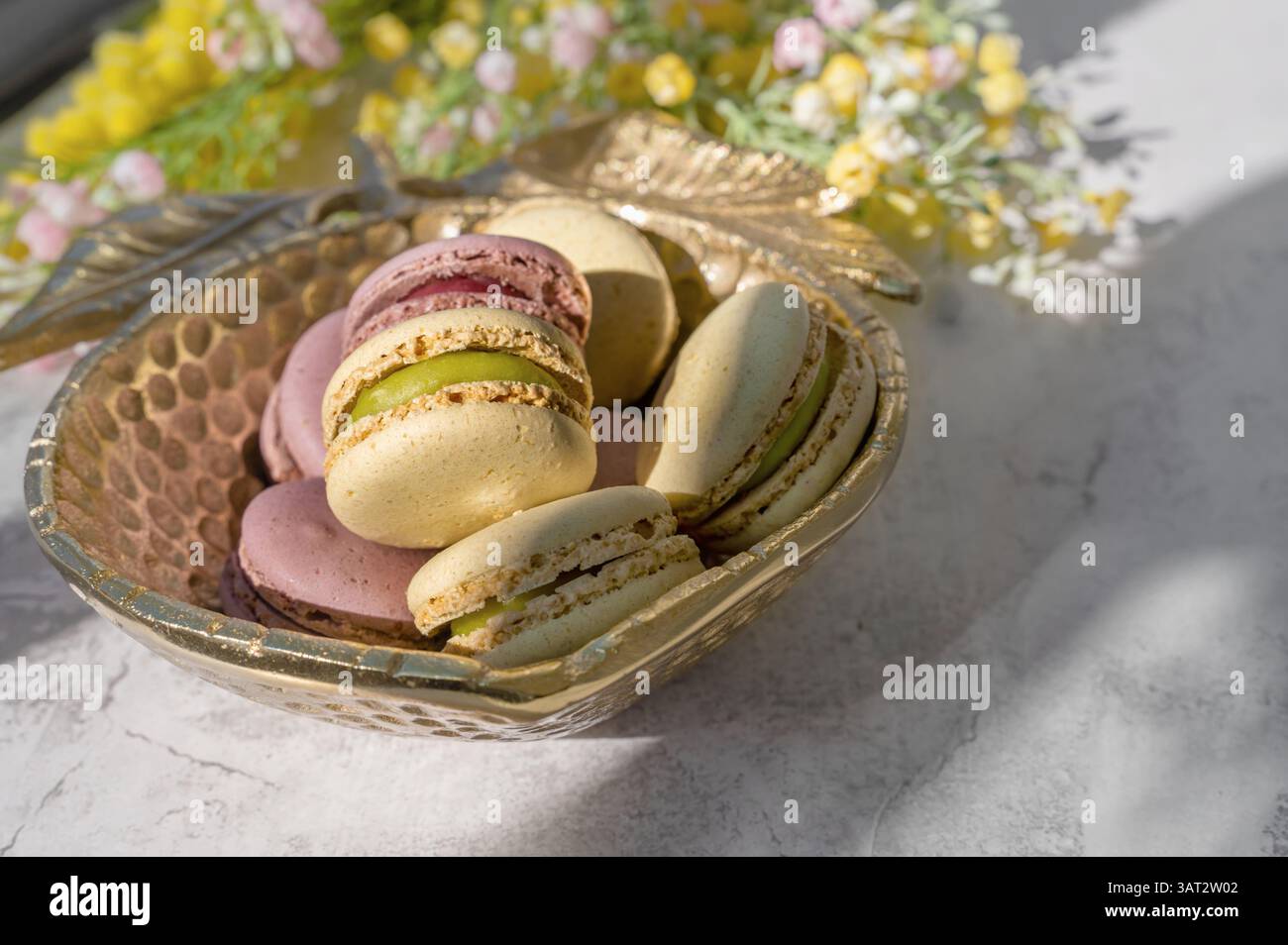 Colorful macarons are elegantly placed in a gold leaf bowl, accompanied ...