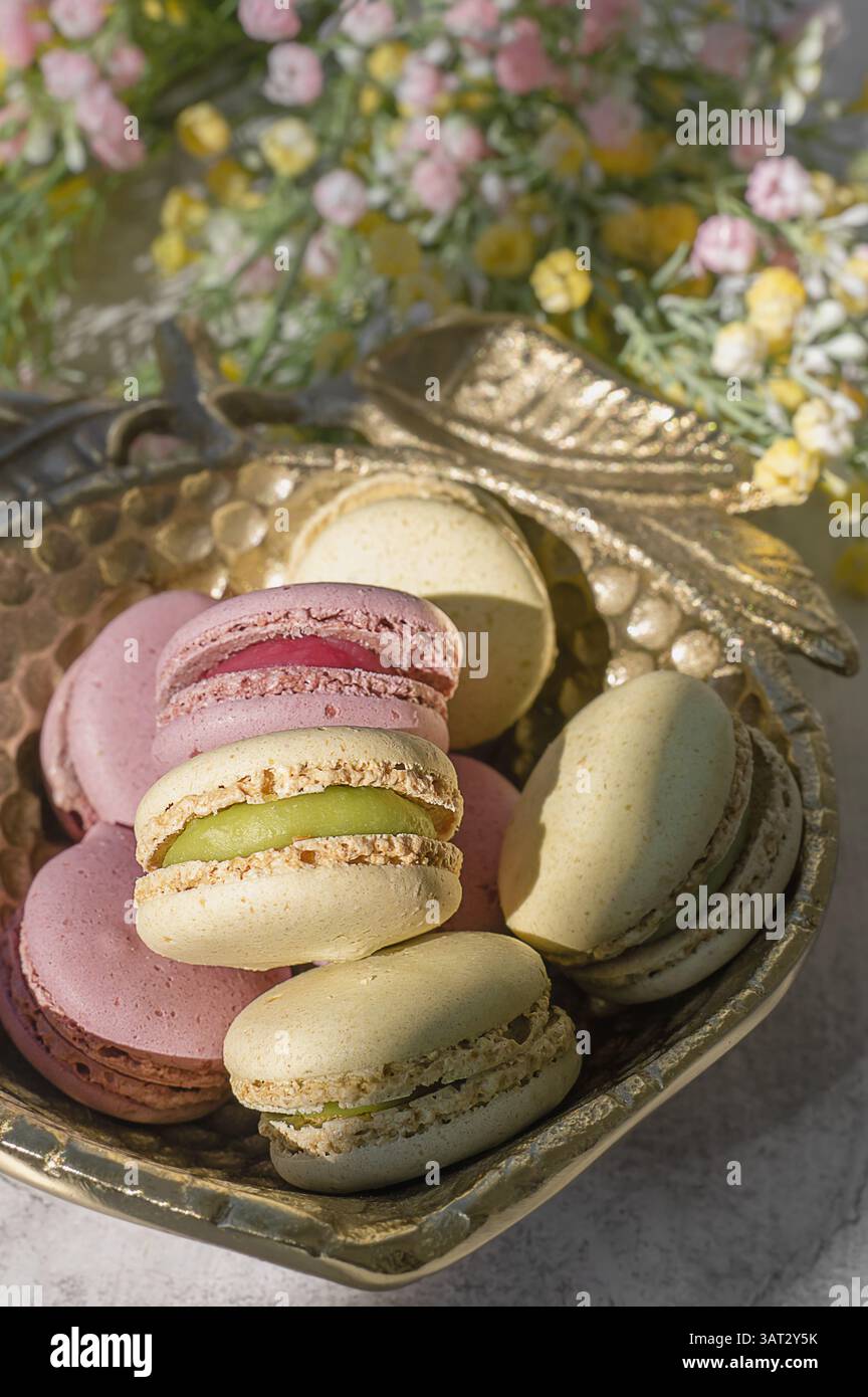 Colorful macarons are elegantly placed in a gold leaf bowl, accompanied ...