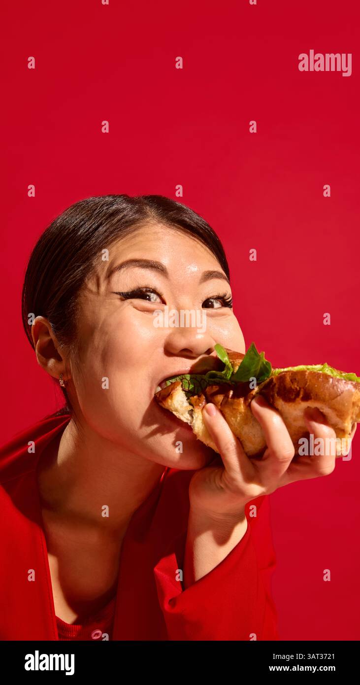 Happy Asian woman biting delicious sandwich with joy, wide-eyed and ...
