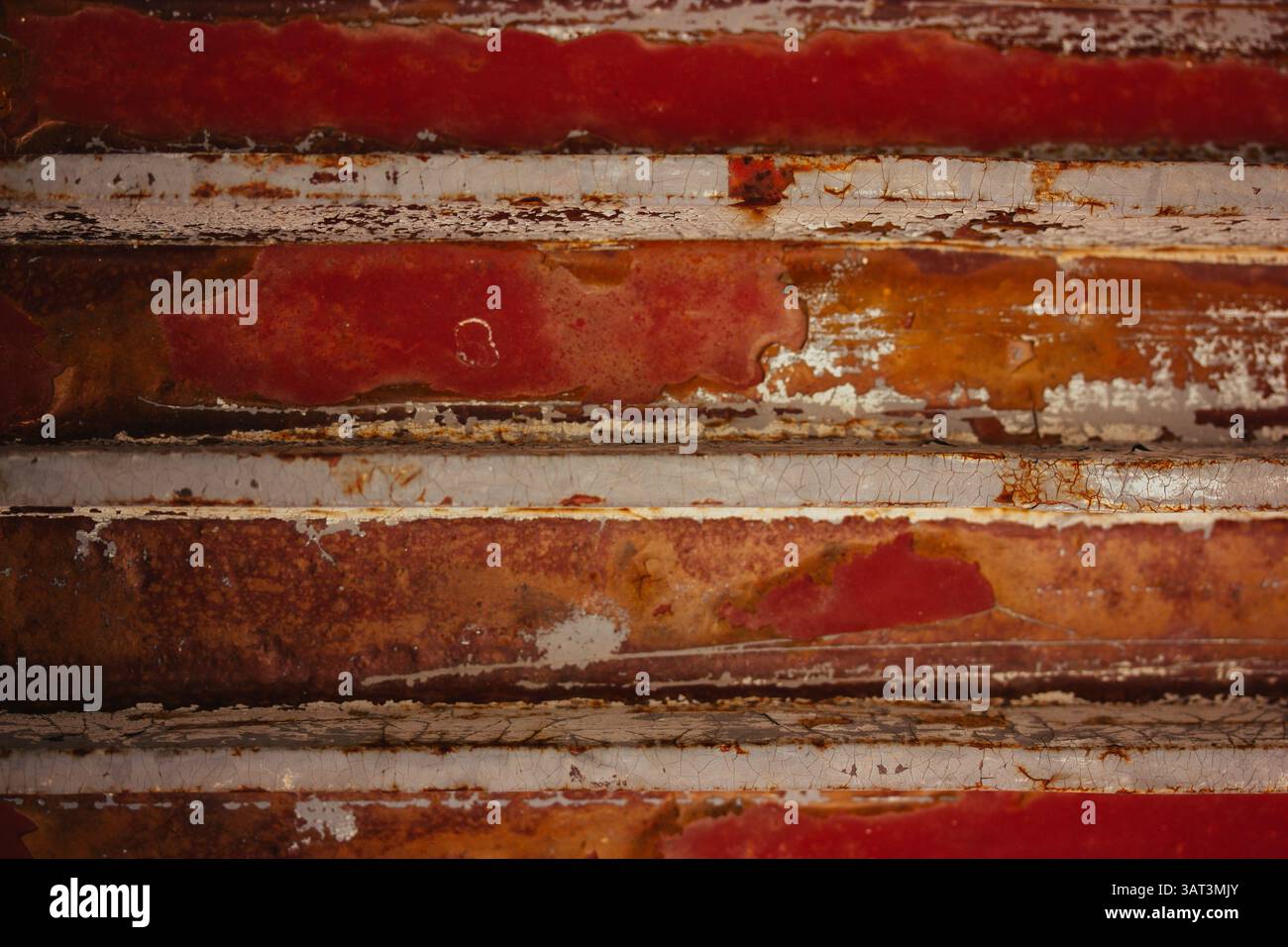 Detailed view of aged, peeling red and white paint, revealing textured rust underneath the ...