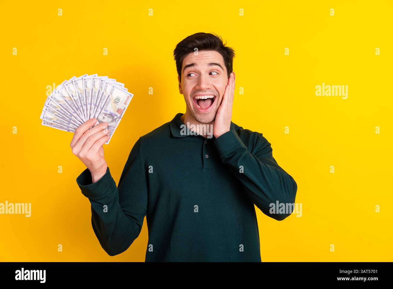 Excited young man holding cash and expressing surprise against a bright ...
