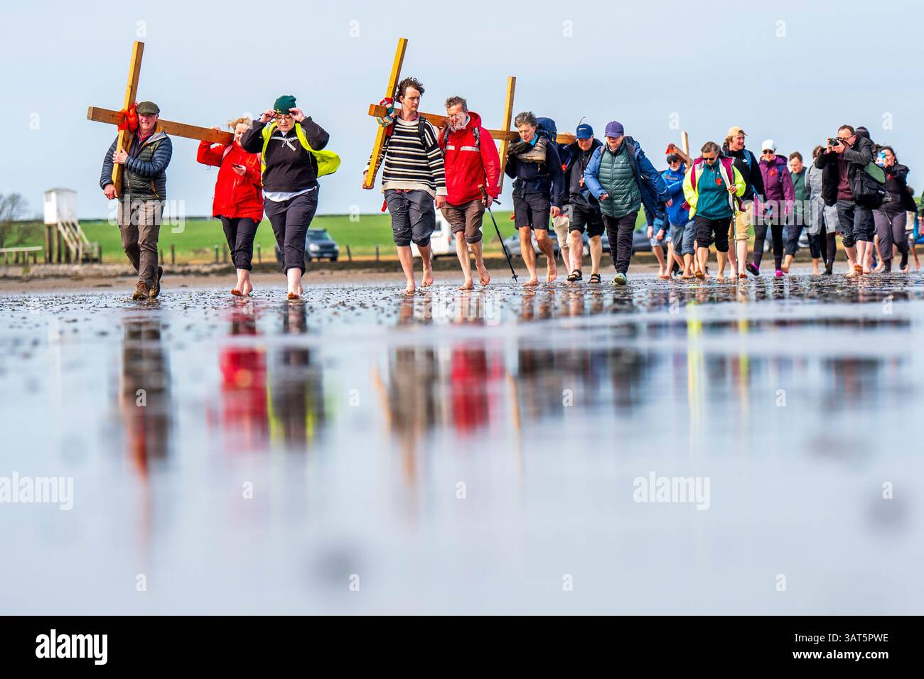 Pilgrims carrying wooden crosses cross the sands at low tide to the ...