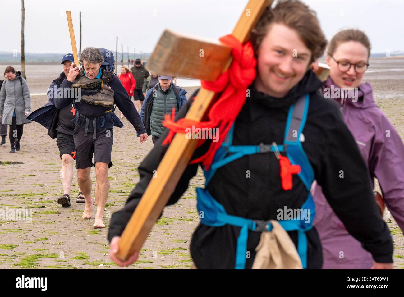 Pilgrims carrying wooden crosses cross the sands at low tide to the ...