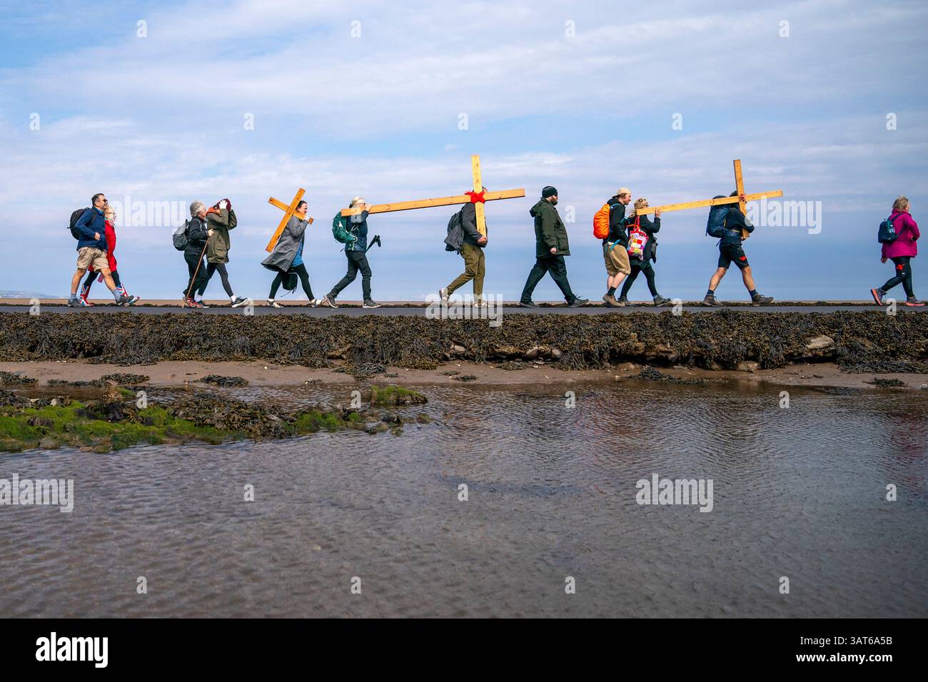 Pilgrims carrying wooden crosses cross the sands at low tide to the ...