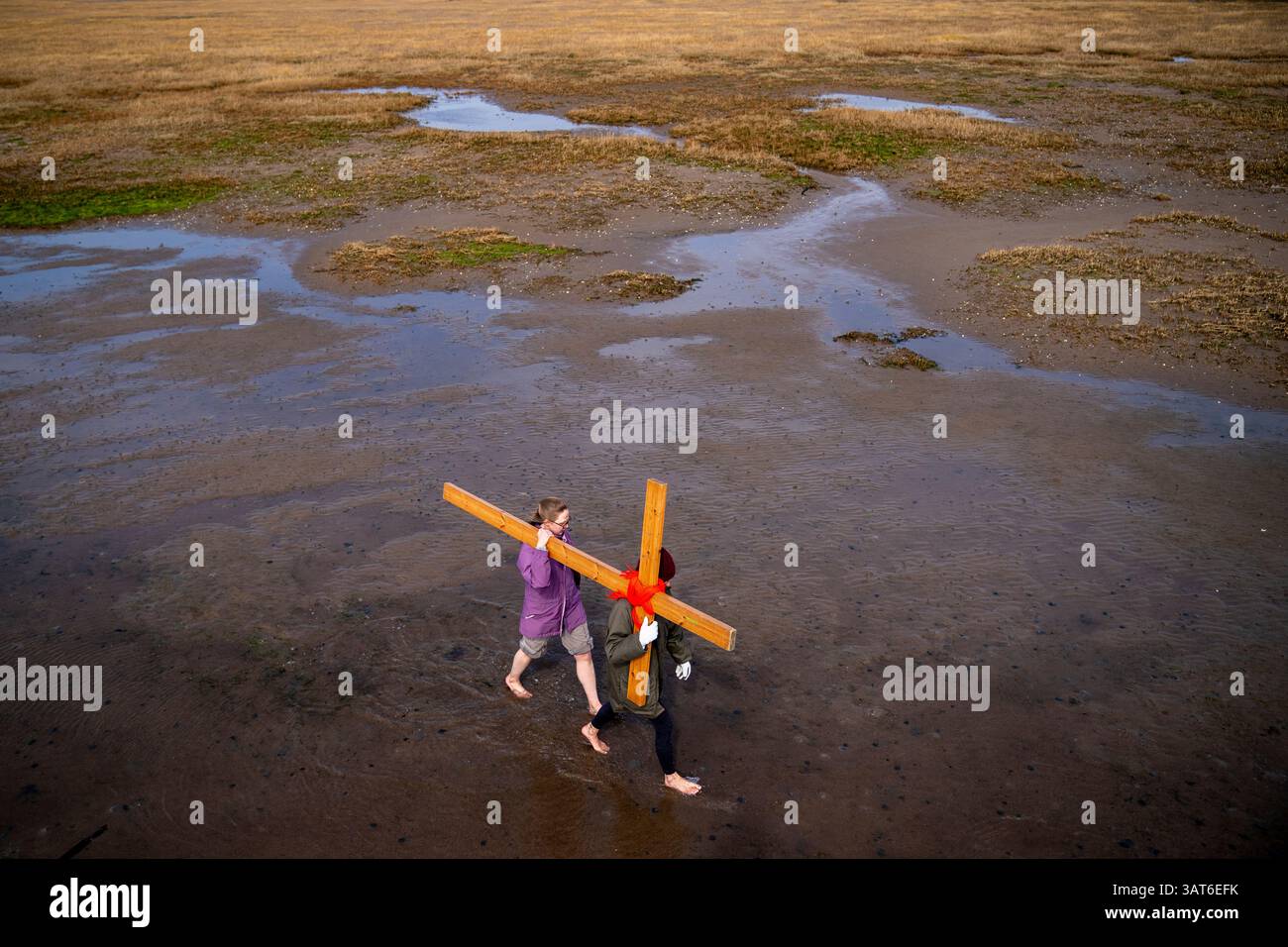 Pilgrims carrying wooden crosses cross the sands at low tide to the ...