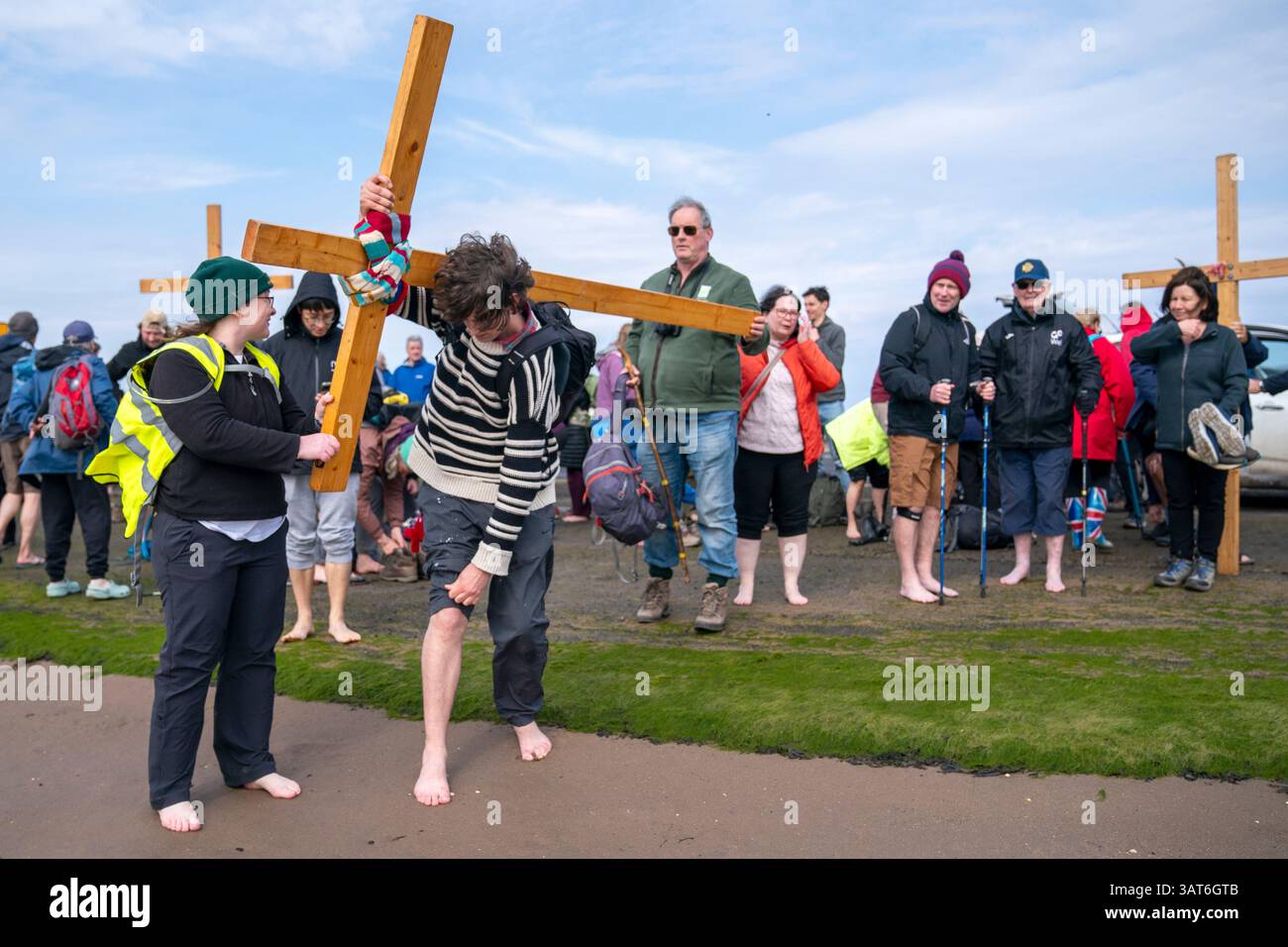 Pilgrims carrying wooden crosses prepare to cross the sands at low tide ...