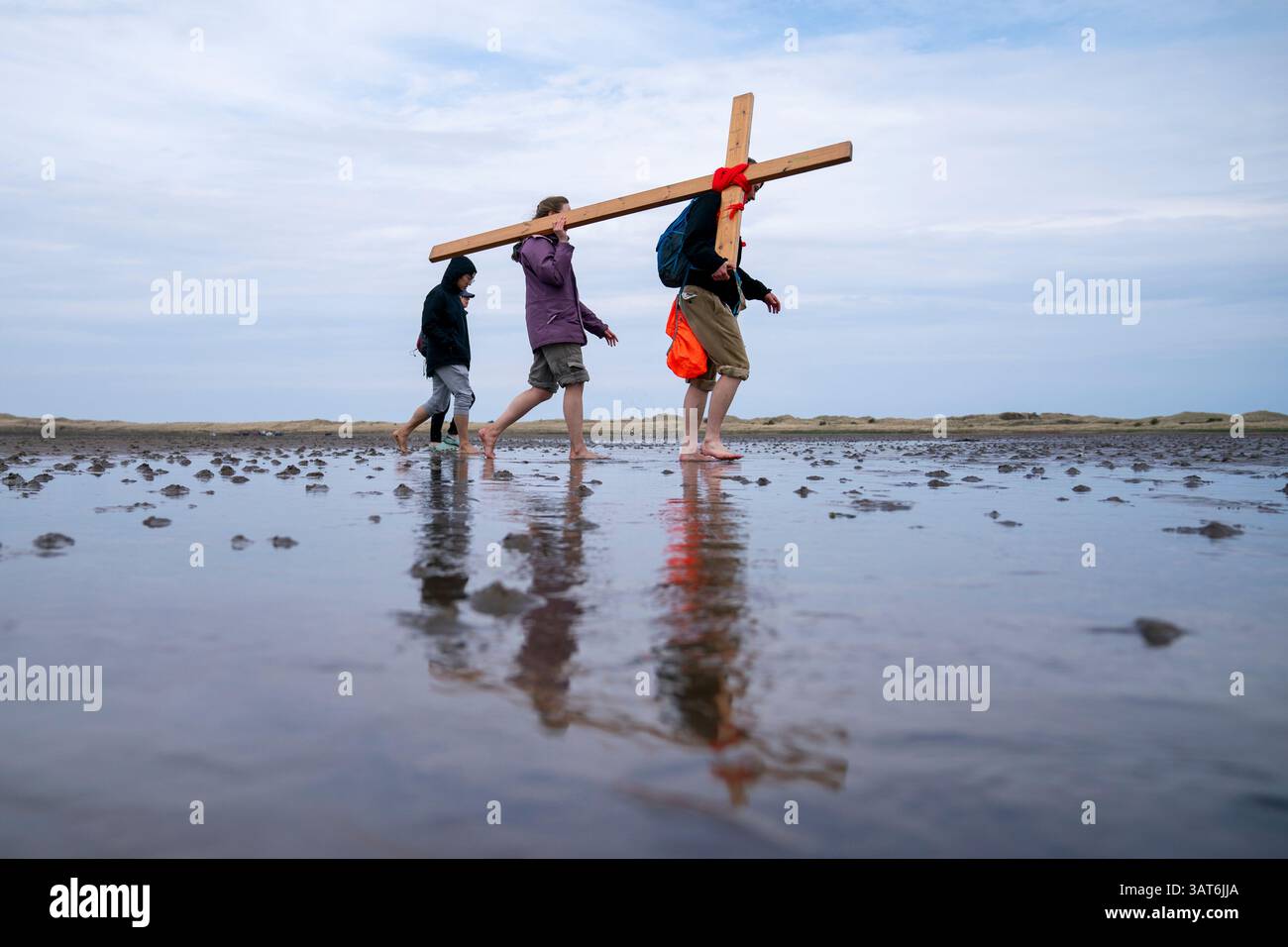 Pilgrims carrying wooden crosses cross the sands at low tide to the ...