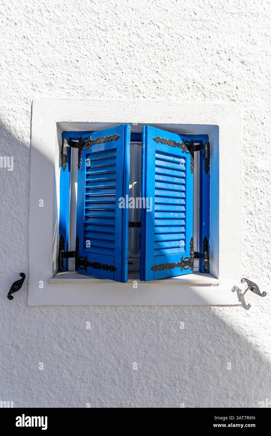 Detail of a sunlit Cycladic window with vivid blue shutters and ornate ...