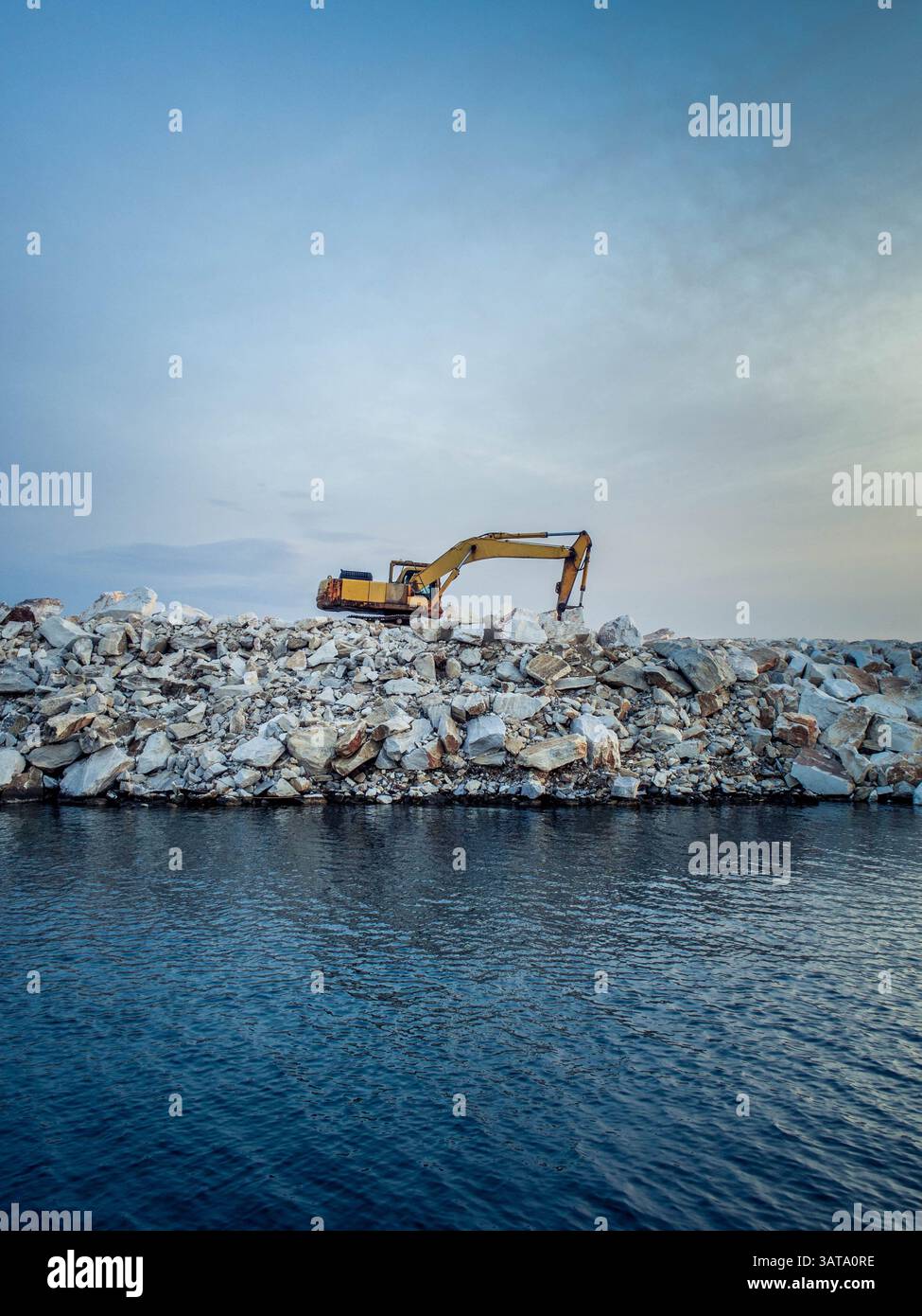 Side view of a mechanical digger moving rocks to build a seawall Stock ...