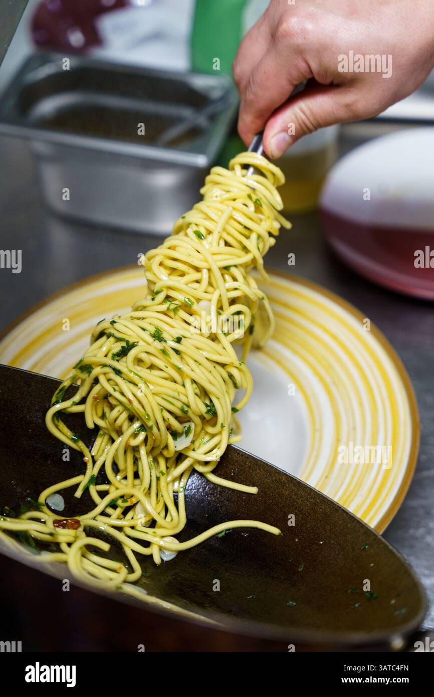 A chef carefully plates a serving of spaghetti aglio e olio using tongs ...