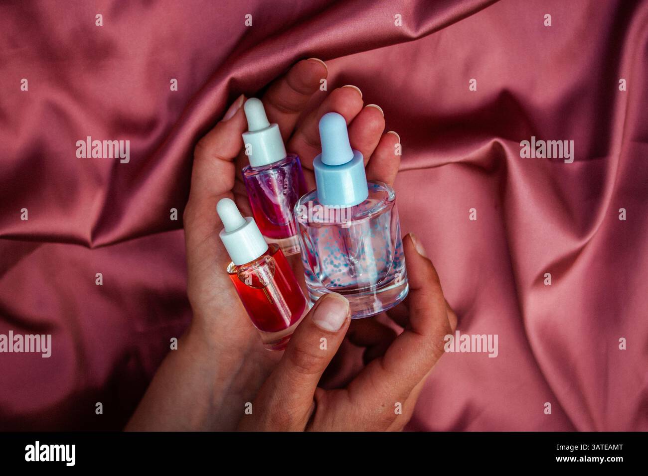 Cosmetic dropper bottles rest delicately in open female hands on a soft ...