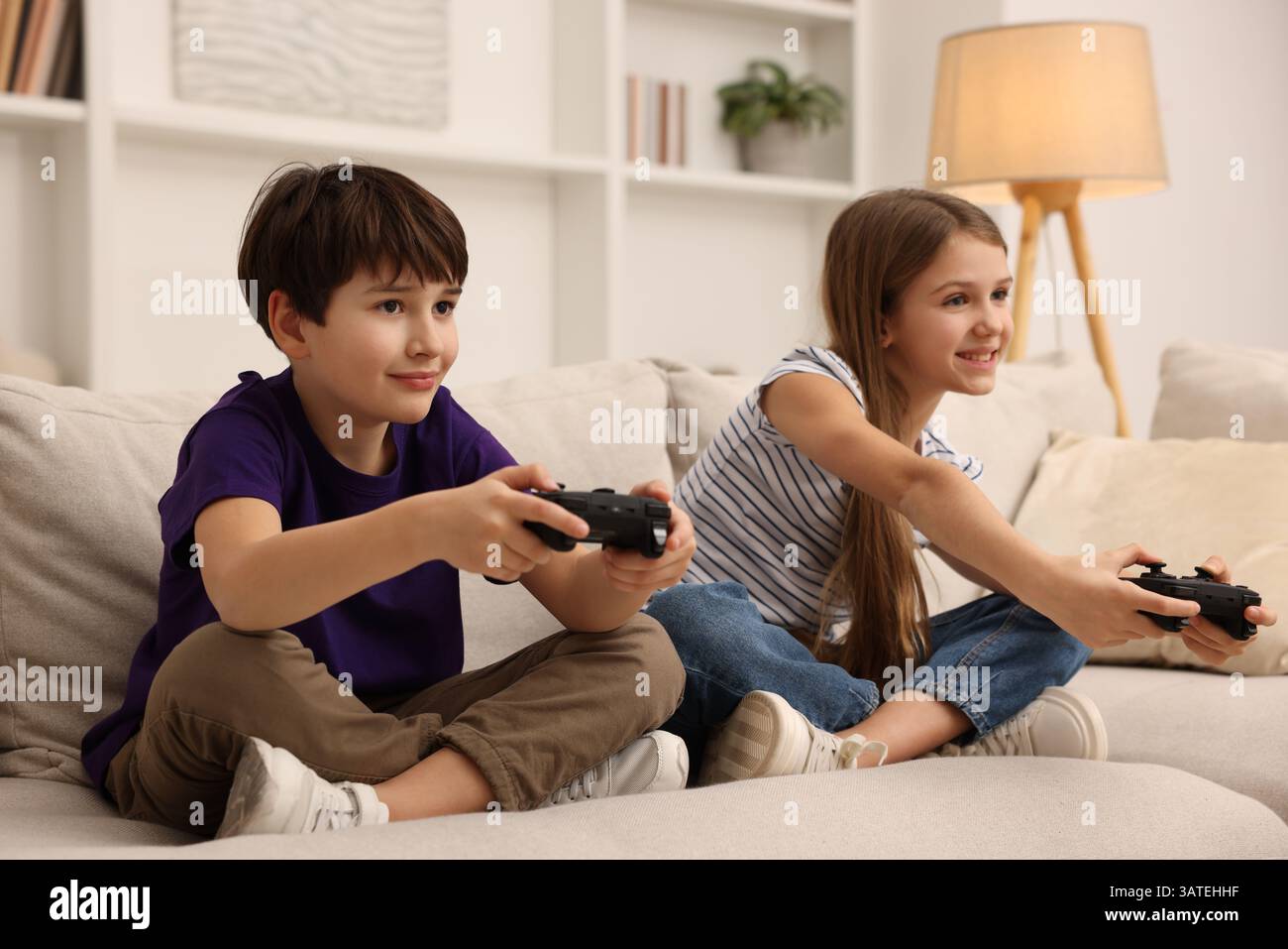 Cute kids playing video games on sofa in living room Stock Photo - Alamy