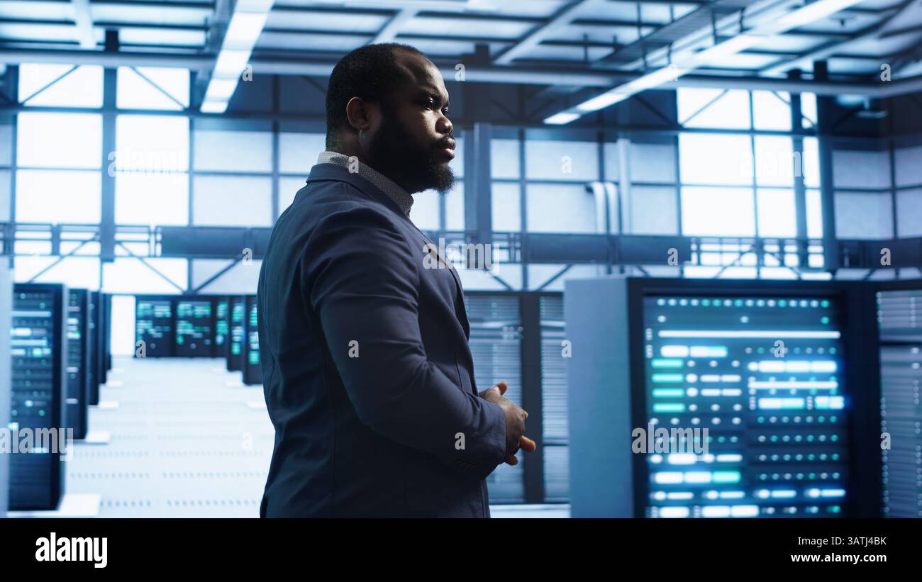 African american technician walking in data center, monitoring systems to identify errors. Man ...