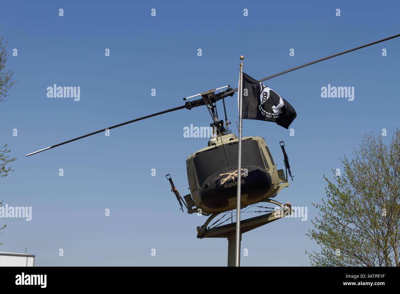 A military-green Huey helicopter mounted on a pole, standing tall ...