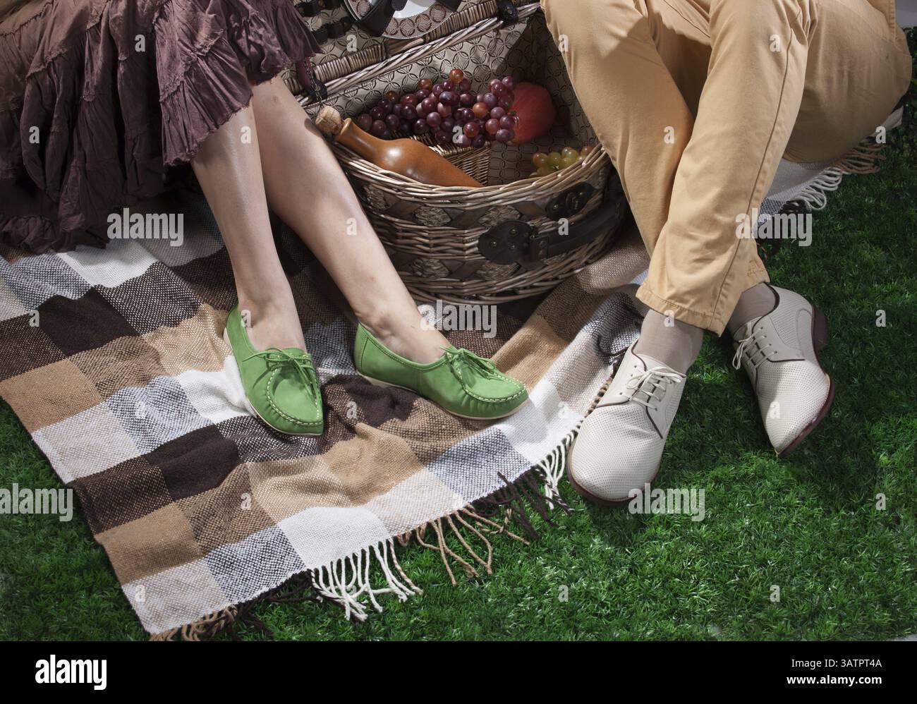 Woman's and man's legs, picnic wicker basket and checkered plaid on a ...