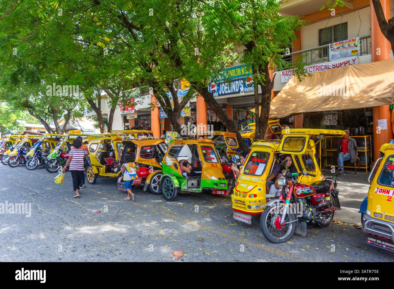 A line of yellow tricycles waits quietly along a tree-lined roadside in ...
