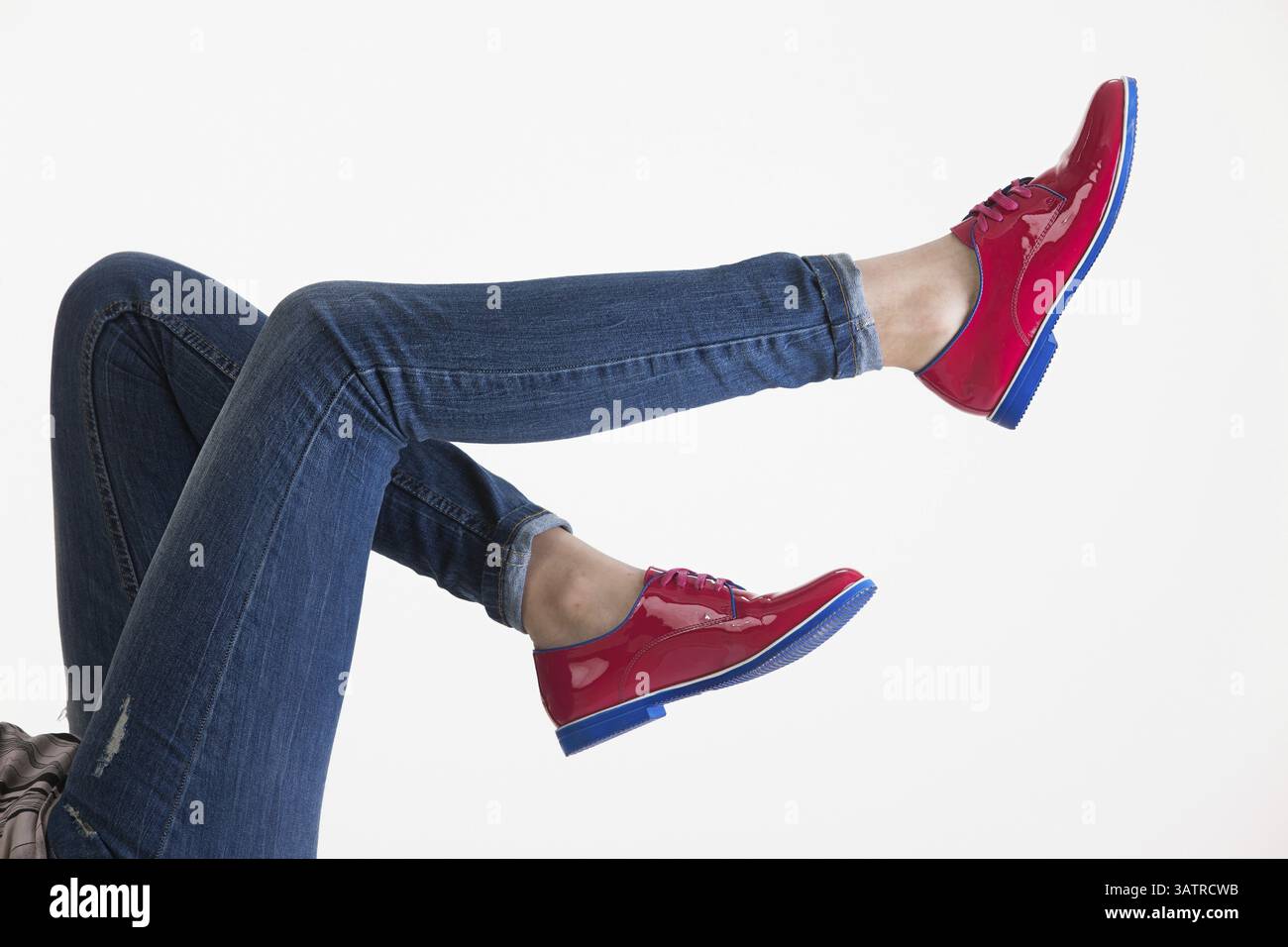 Woman's legs in blue jeans and red shoes isoltaed studio background ...