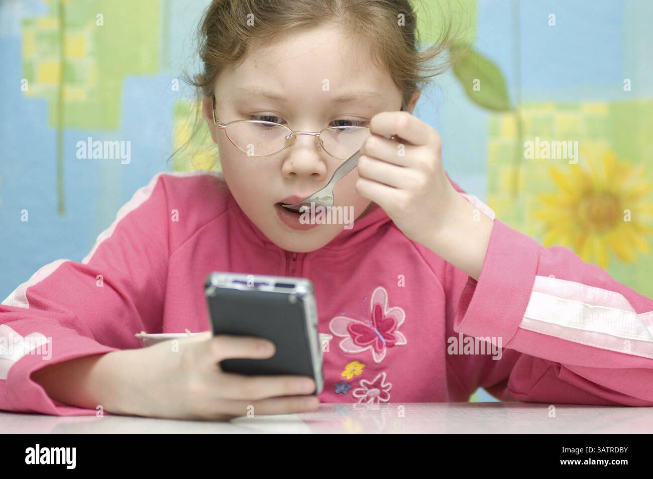 Eight year old girl in pink eats holding a fork in her mouth and ...