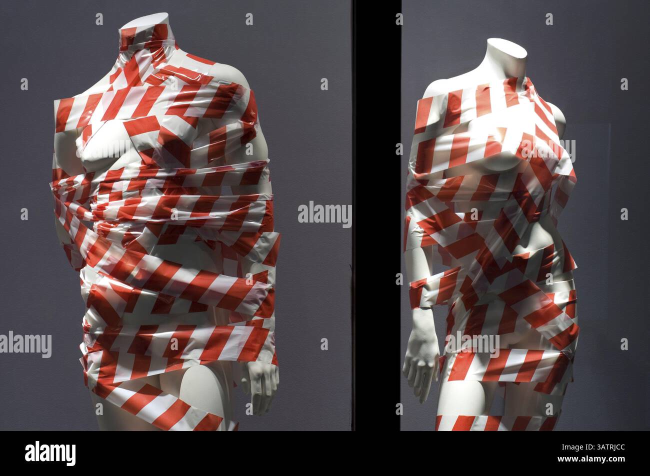Two headless mannequins winded with striped warning tape in shop window ...
