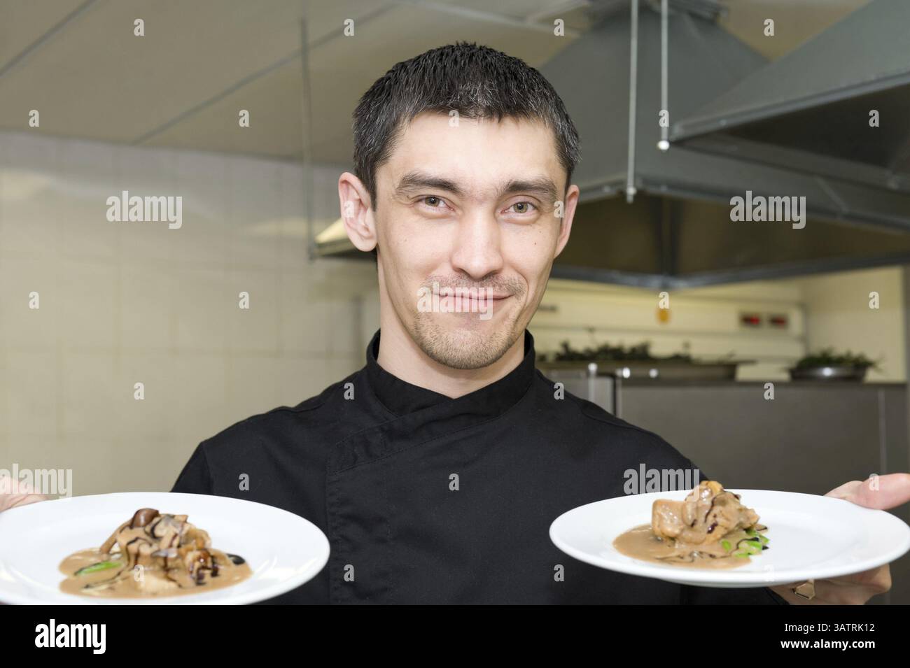 Real male caucasian smiling chef in black uniform holds plates with ...