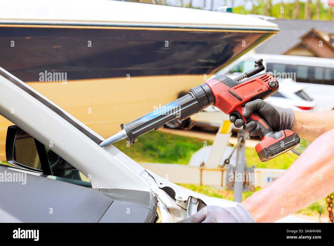 Worker uses caulking gun to repair vehicle windshield beside parked ...