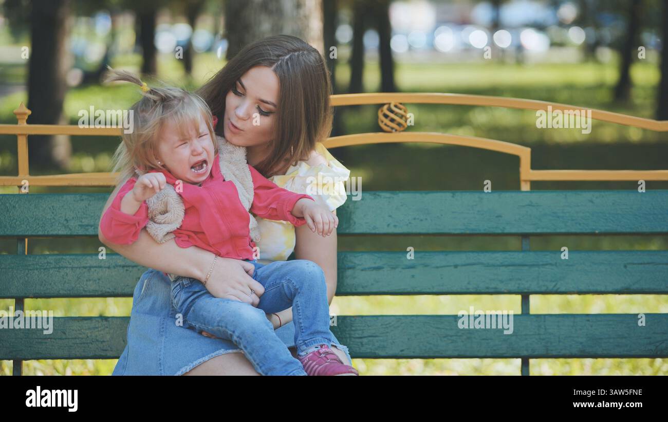 Nurturing mother soothing crying infant while seated on park bench ...