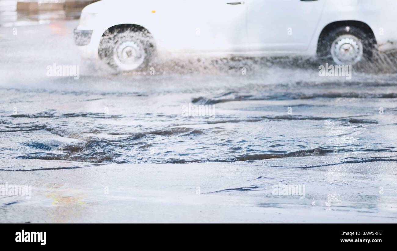 Speeding white vehicle splashing through large roadside puddle ...