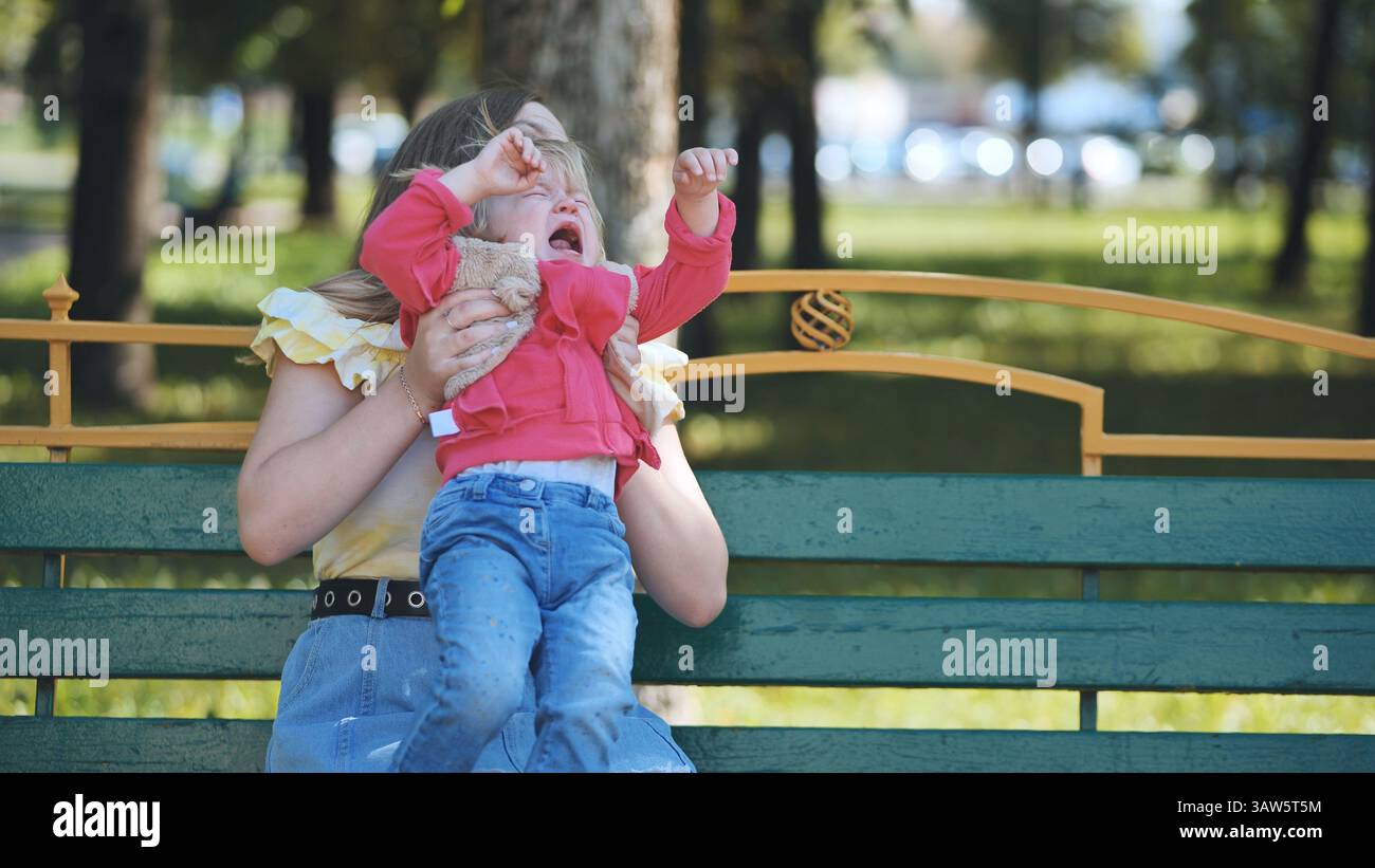 Caring mother comforting weeping child on park bench during bright ...