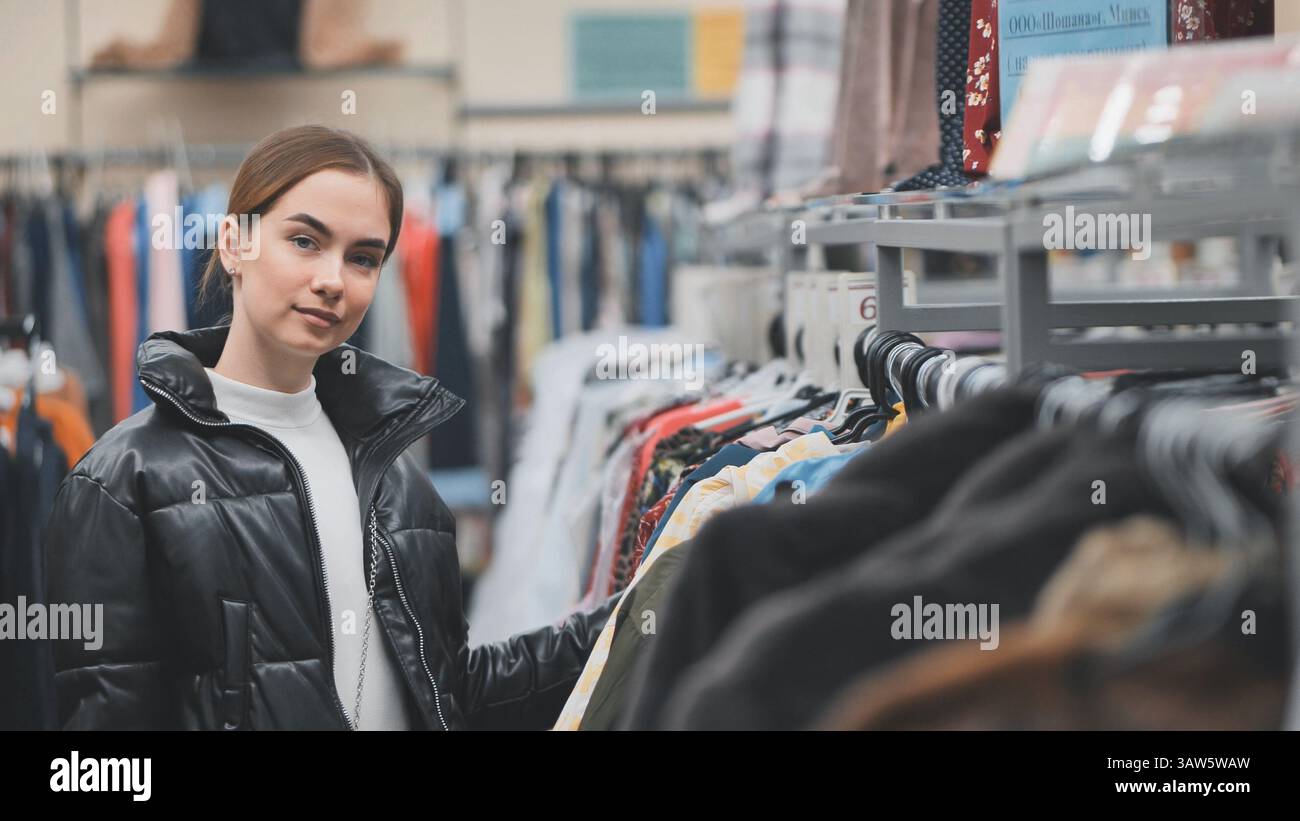 Young shopper searching clothing rack, scanning secondhand garments for ...