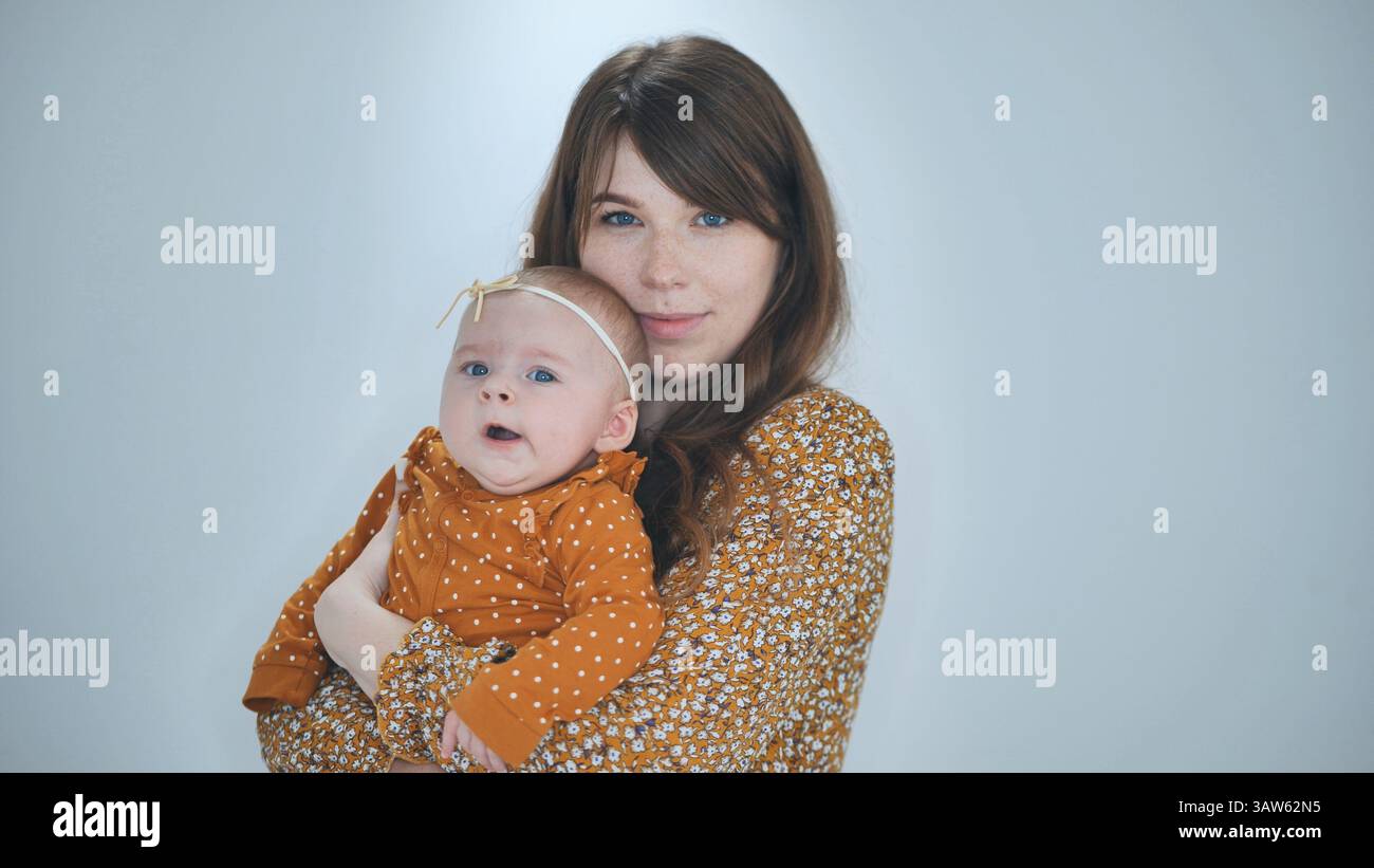 Mother gently cradling infant daughter in coordinating orange clothing ...