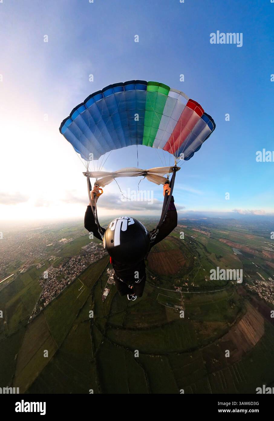 Skydiver flying with parachute over green countryside, wearing helmet ...