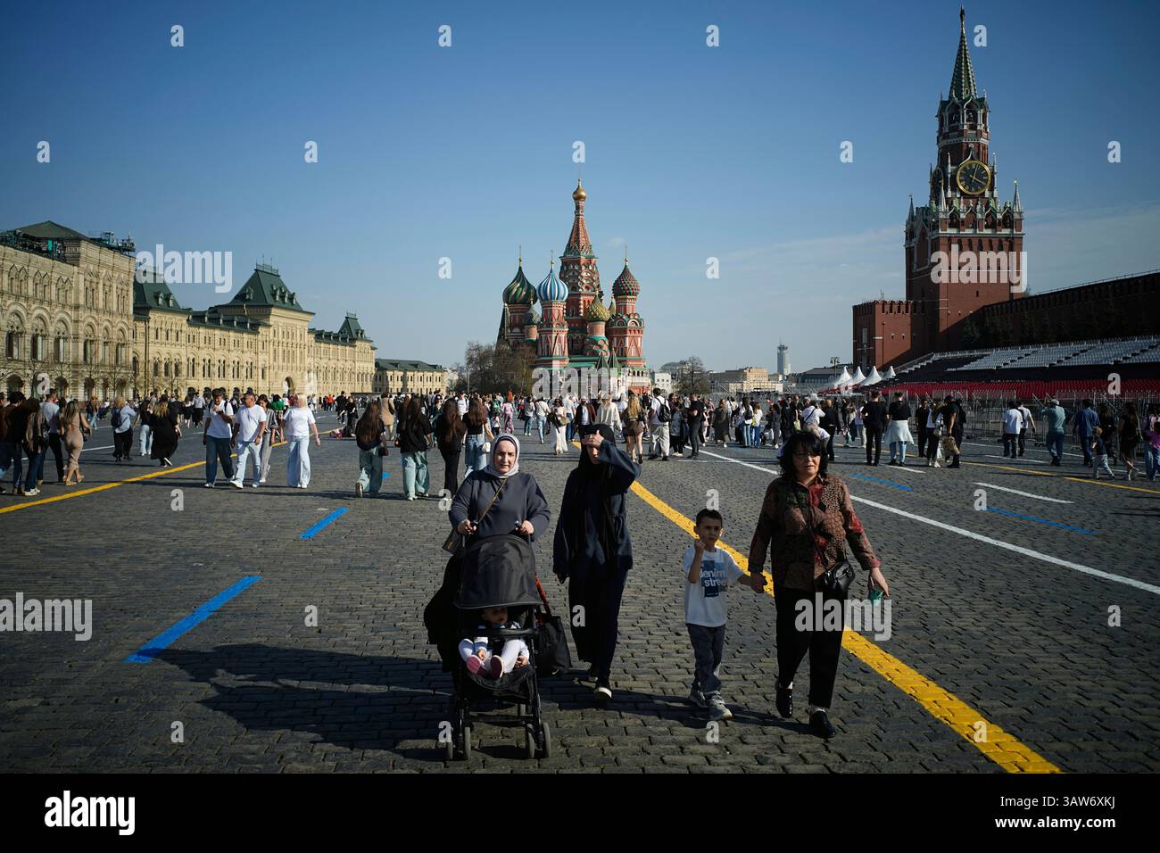People walk at the Red square on a sunny day as the temperature reached ...