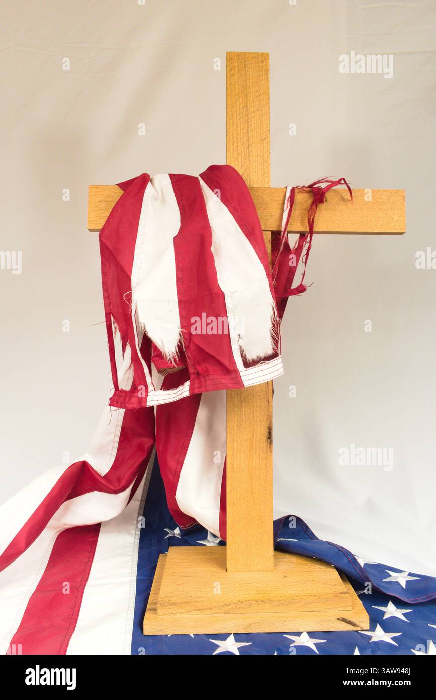 A wooden cross draped with a torn and tattered American flag symbolizes ...