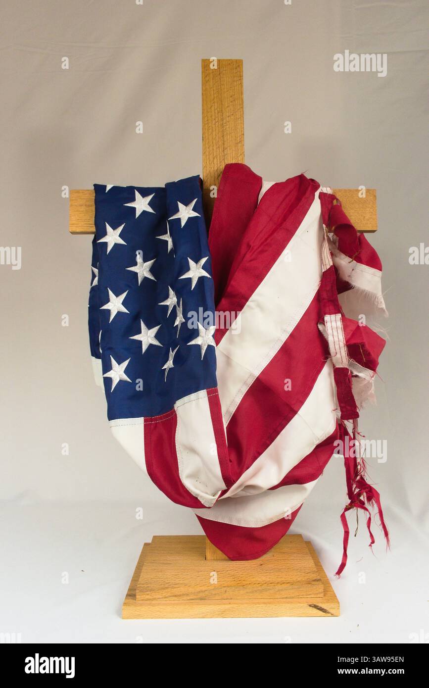 An tattered American flag draped over a wooden cross, symbolizing ...