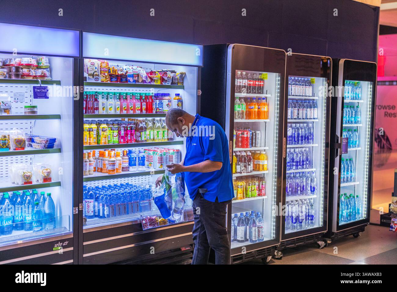 Worker restocking drink shelves in JFK airport shop with refrigerators ...