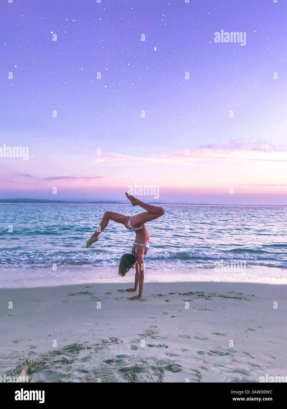 Sporty woman wearing bikini doing an acrobatic yoga pose and handstand ...