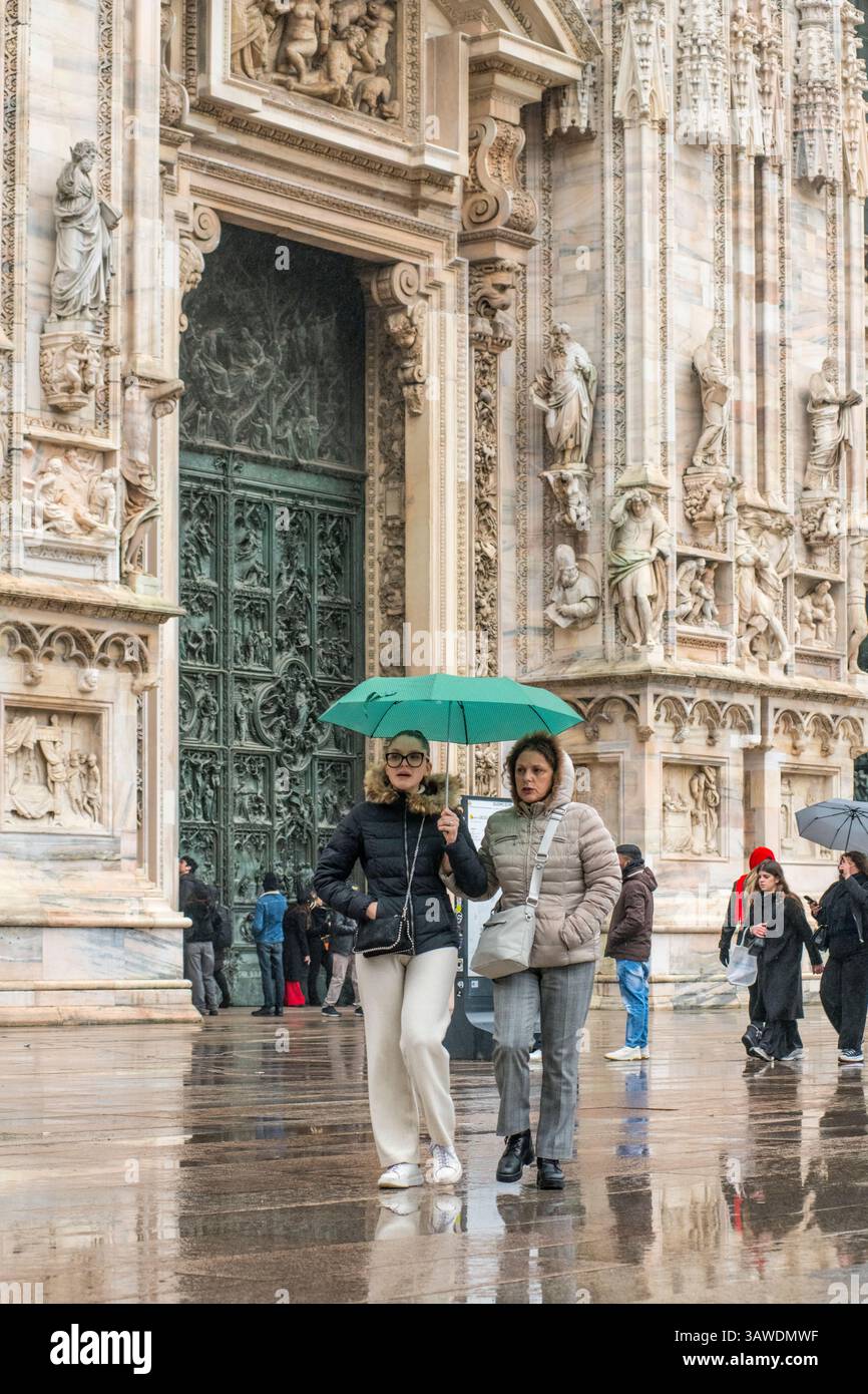 Tourists walking in the rain with umbrella outside Milan Cathedral ...