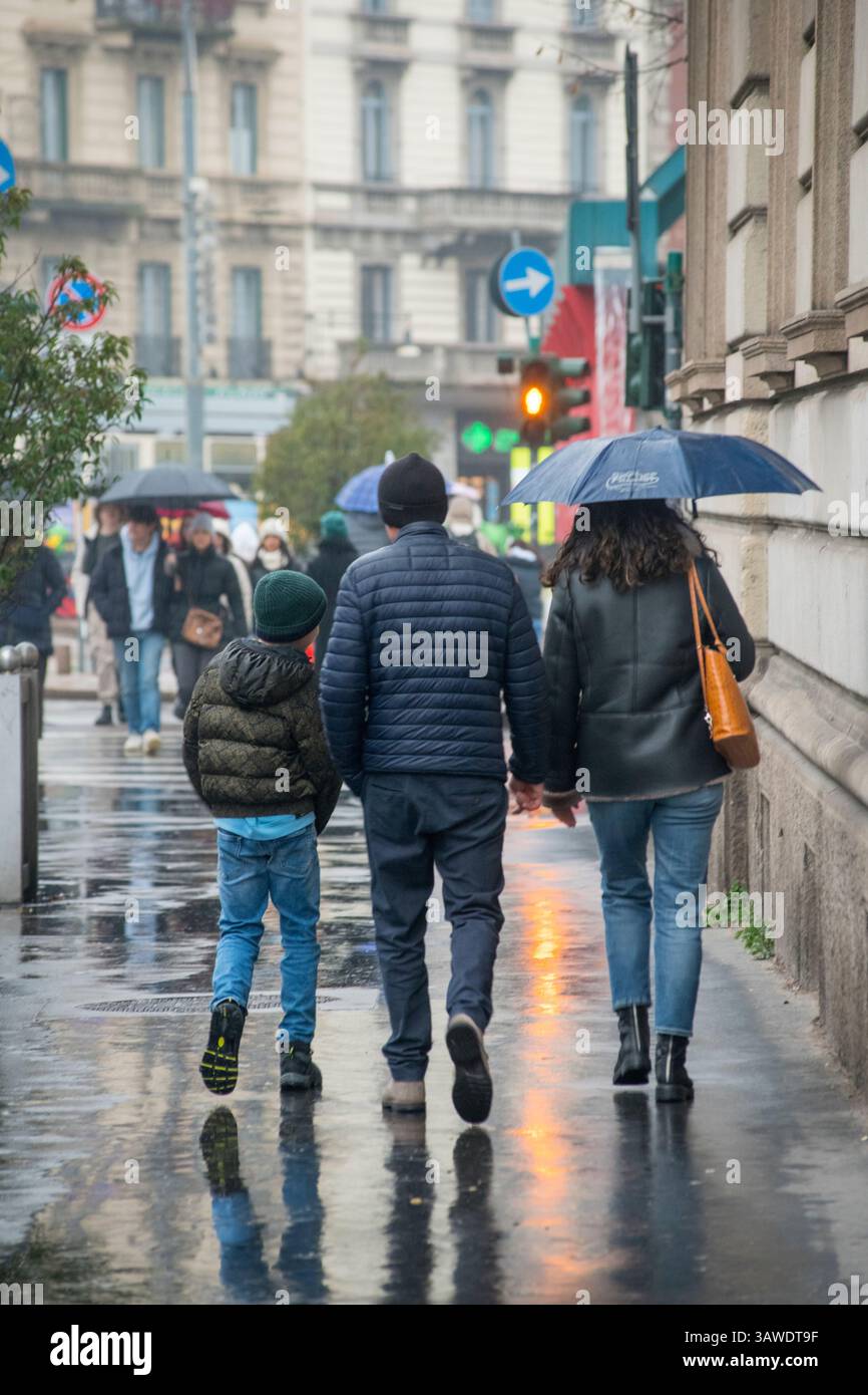 Parents and child walking in the street in the rain, central Milan ...