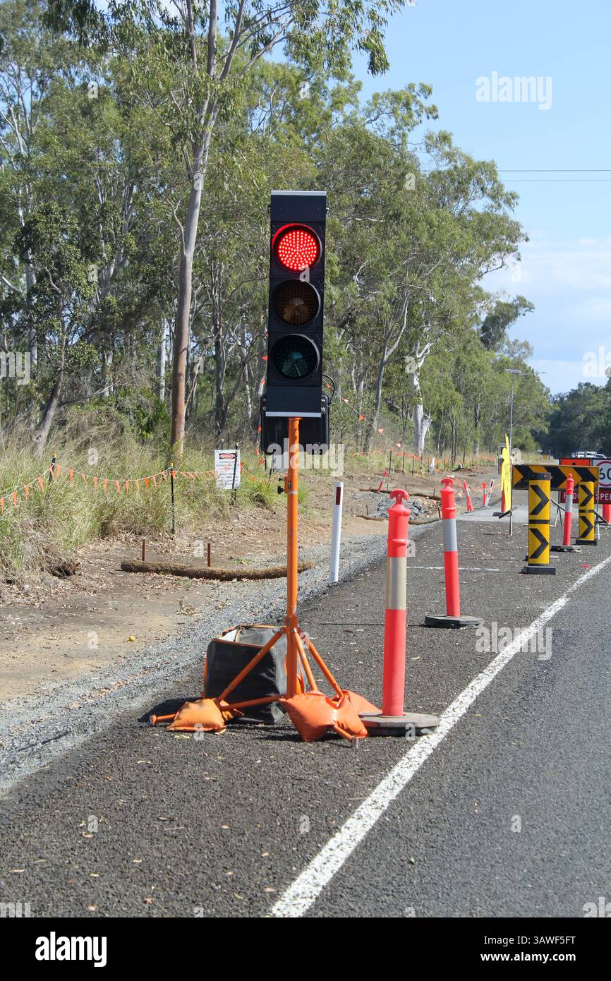 Red traffic light on the side of a highway road surrounded by trees ...