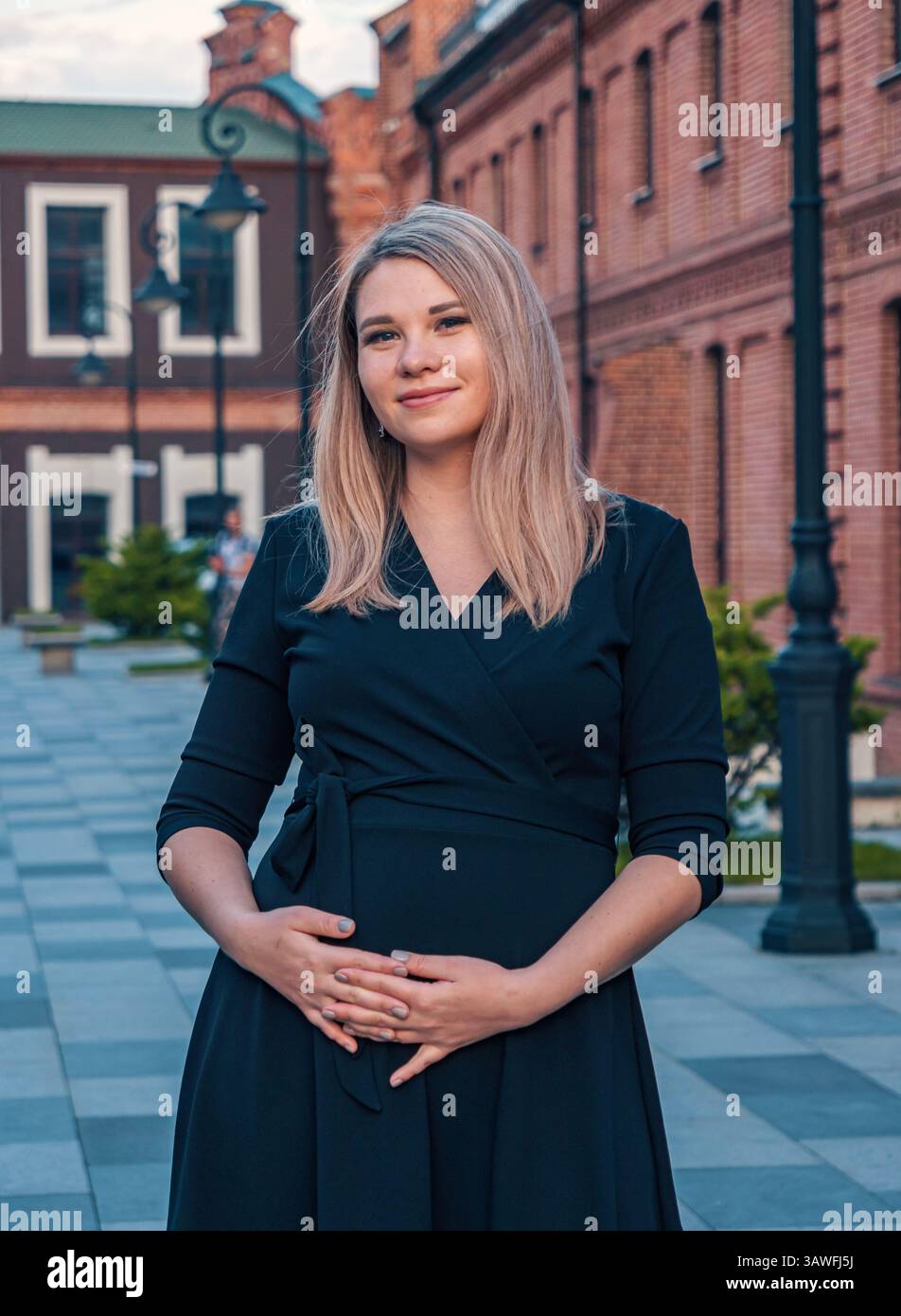 Pregnant woman in a black dress poses confidently outside historic red ...