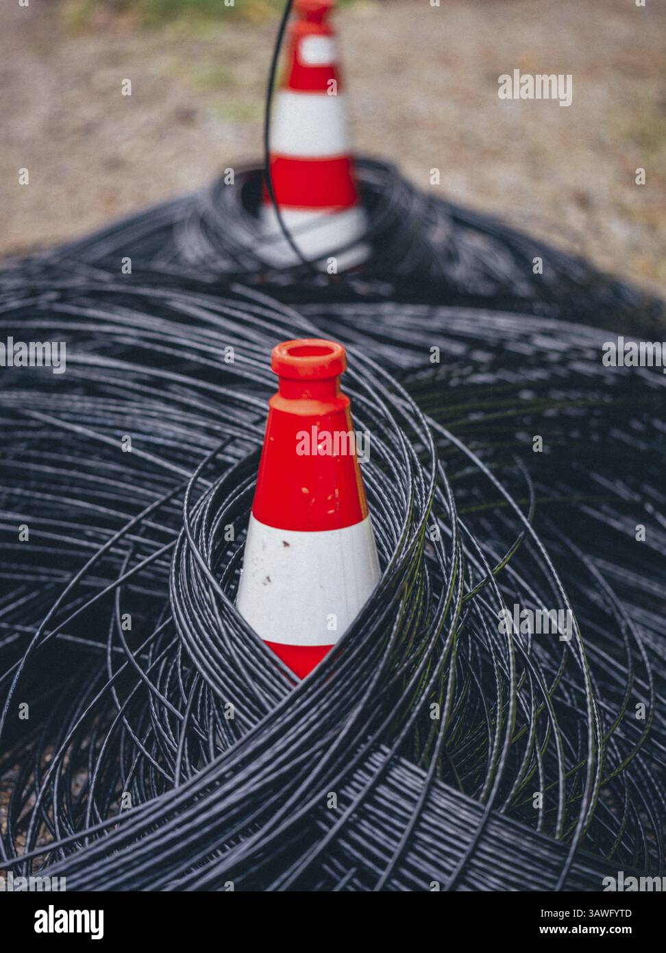 Two red traffic cones between intertwined black cables create an ...