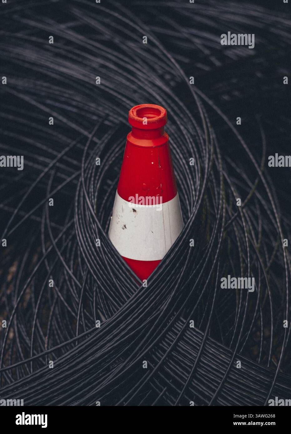 A red traffic cone surrounded by tangled black cables creates a ...