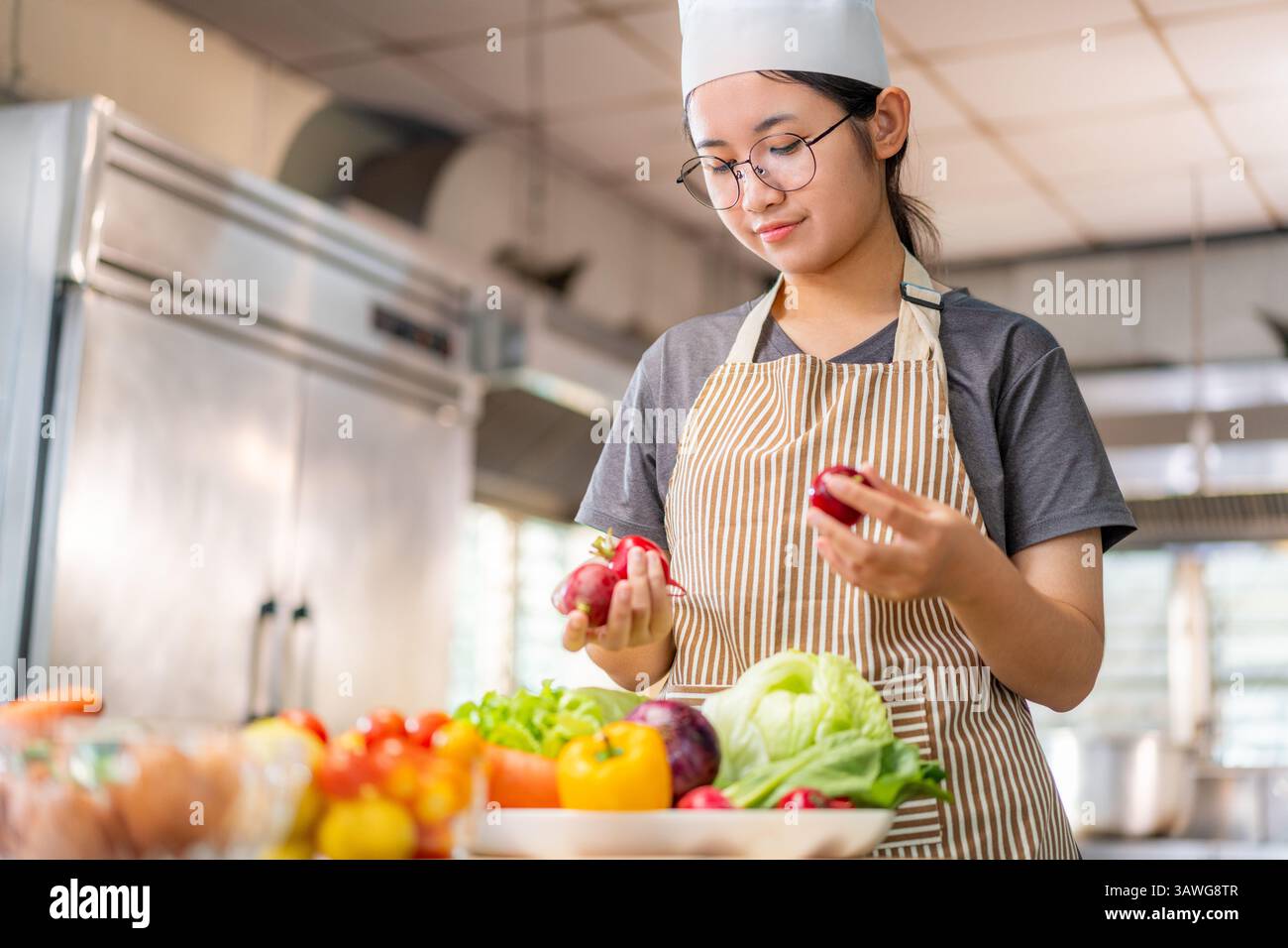 A young female chef wearing a striped apron and chef hat preparing ...