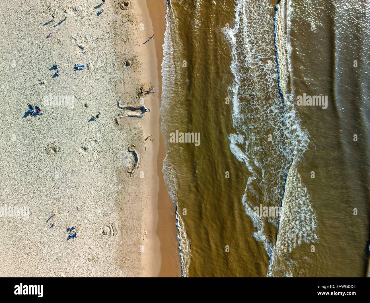 Aerial view of a beach where gentle waves meet the sandy shore. People ...