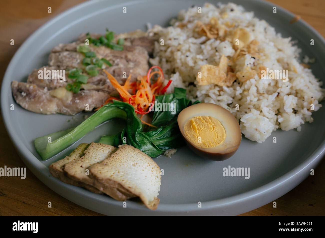 A plate of hainan chicken rice served with bok choy, egg and other ...