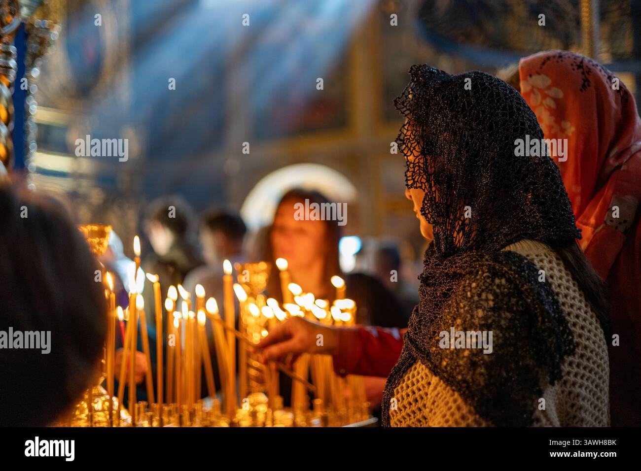 A woman draped in a black lace veil stands in prayer as sunlight ...