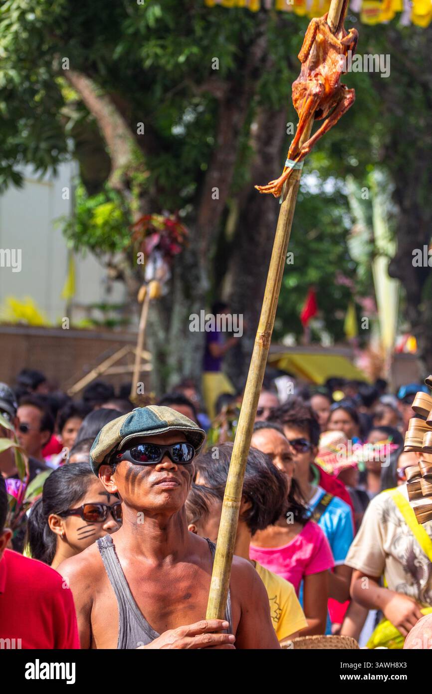 A Filipino man in festive spirit holds a pole with a grilled chicken ...