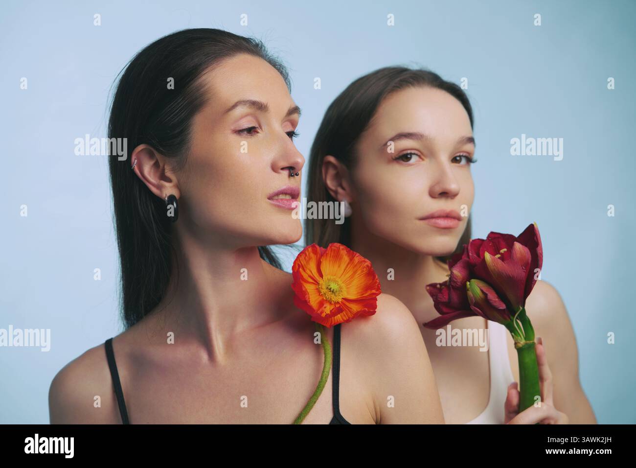 Two women pose with flowers in a studio setting under soft lighting ...