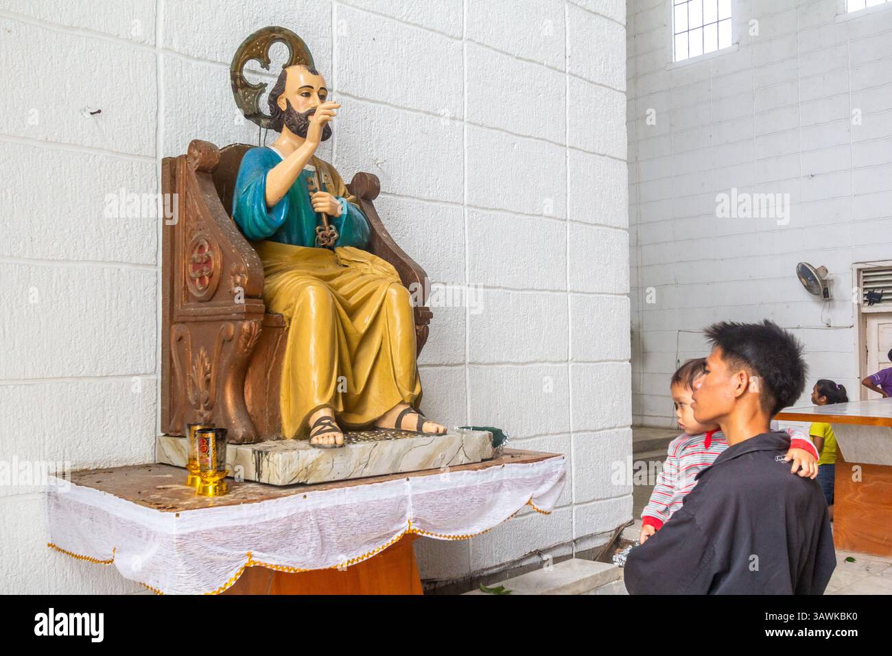 A father carries his child while praying in front of a seated image of ...